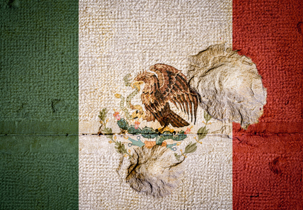 Stone wall with the flag of Mexico and Bullet holes | Español